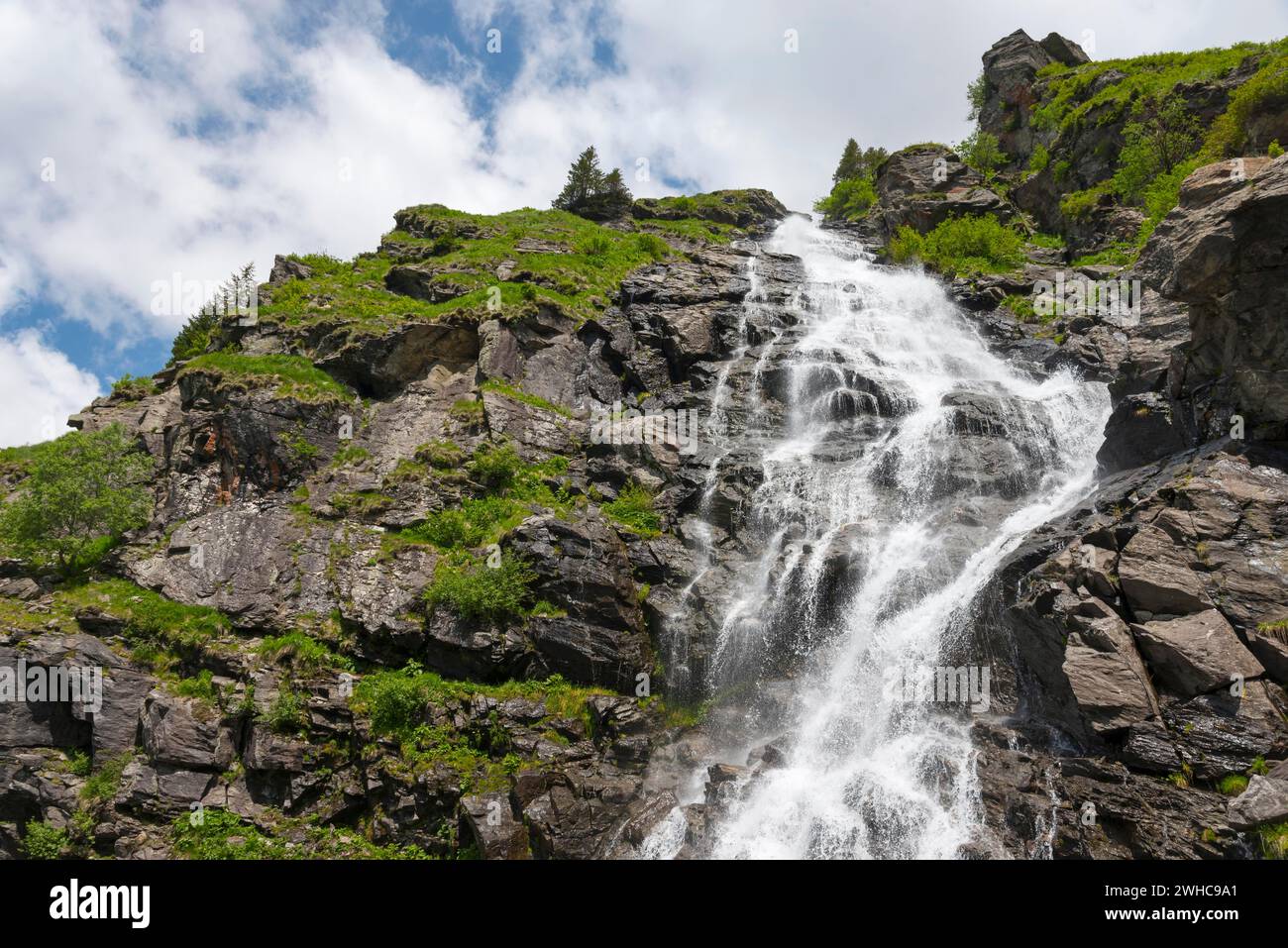 A gushing waterfall cascades over rocky slopes under the blue sky ...