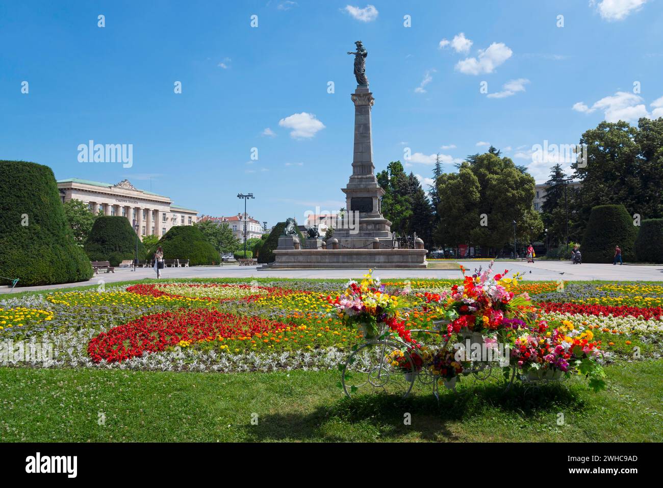 A sunny park with a large monument surrounded by colourful flowerbeds ...
