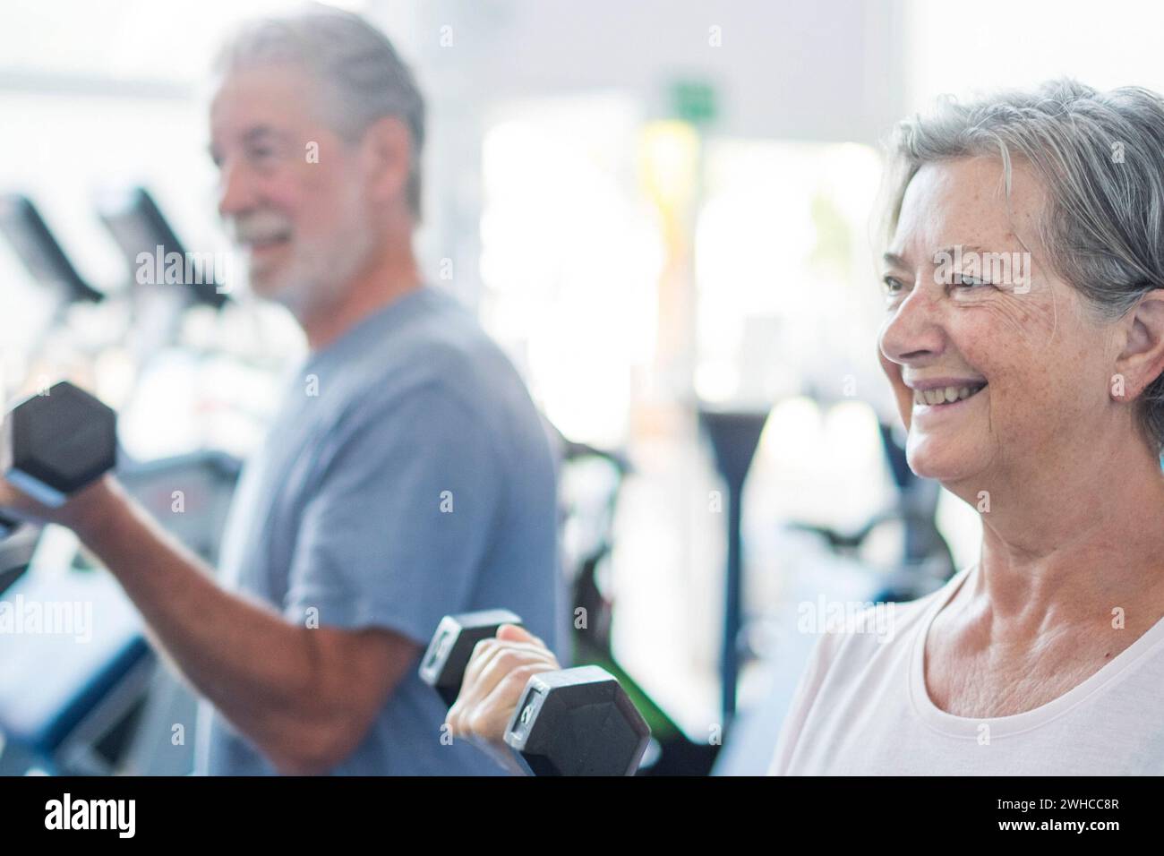 couple of two seniors training together at the gym with dumbbells in ...