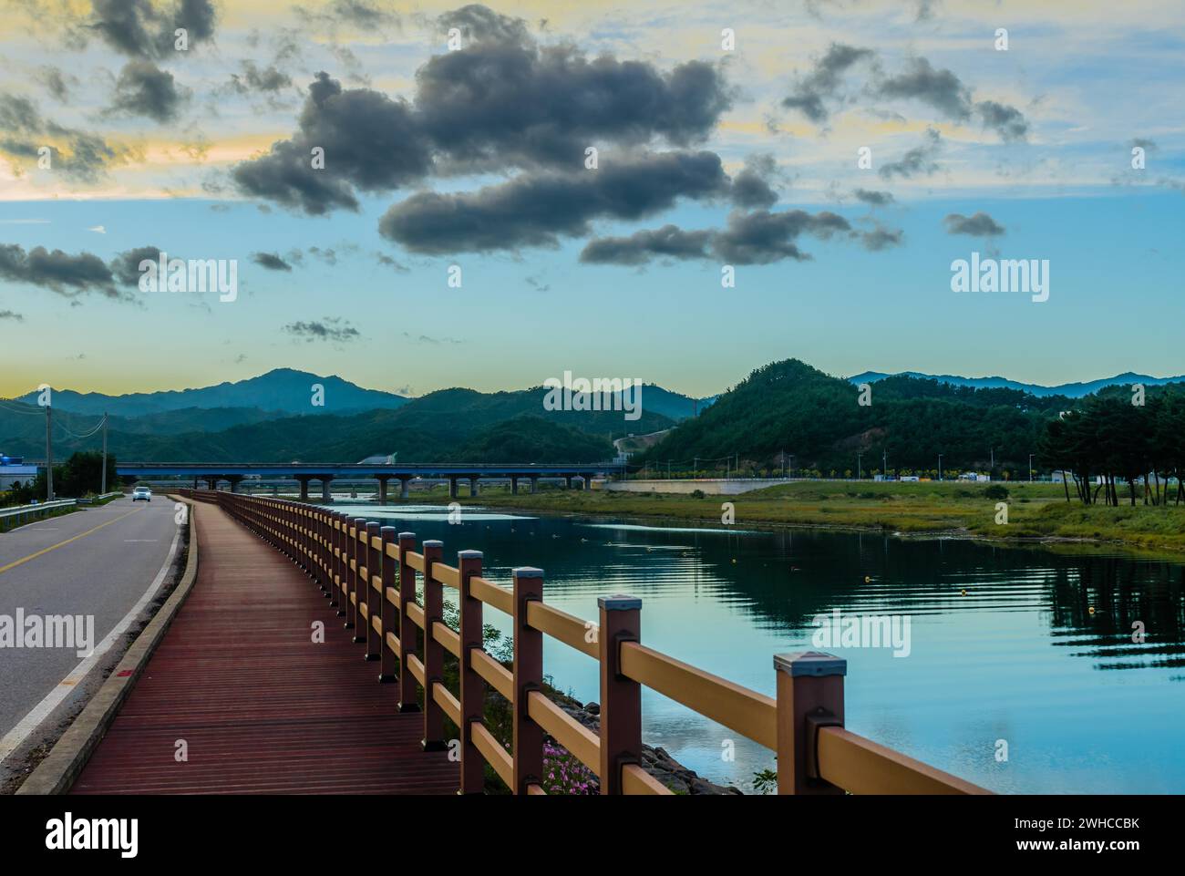 Car traveling on two lane country road along lakeside boardwalk under ...