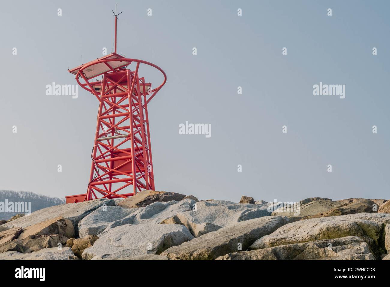 Red steel warning beacon on pier of large boulders at rural fishing ...