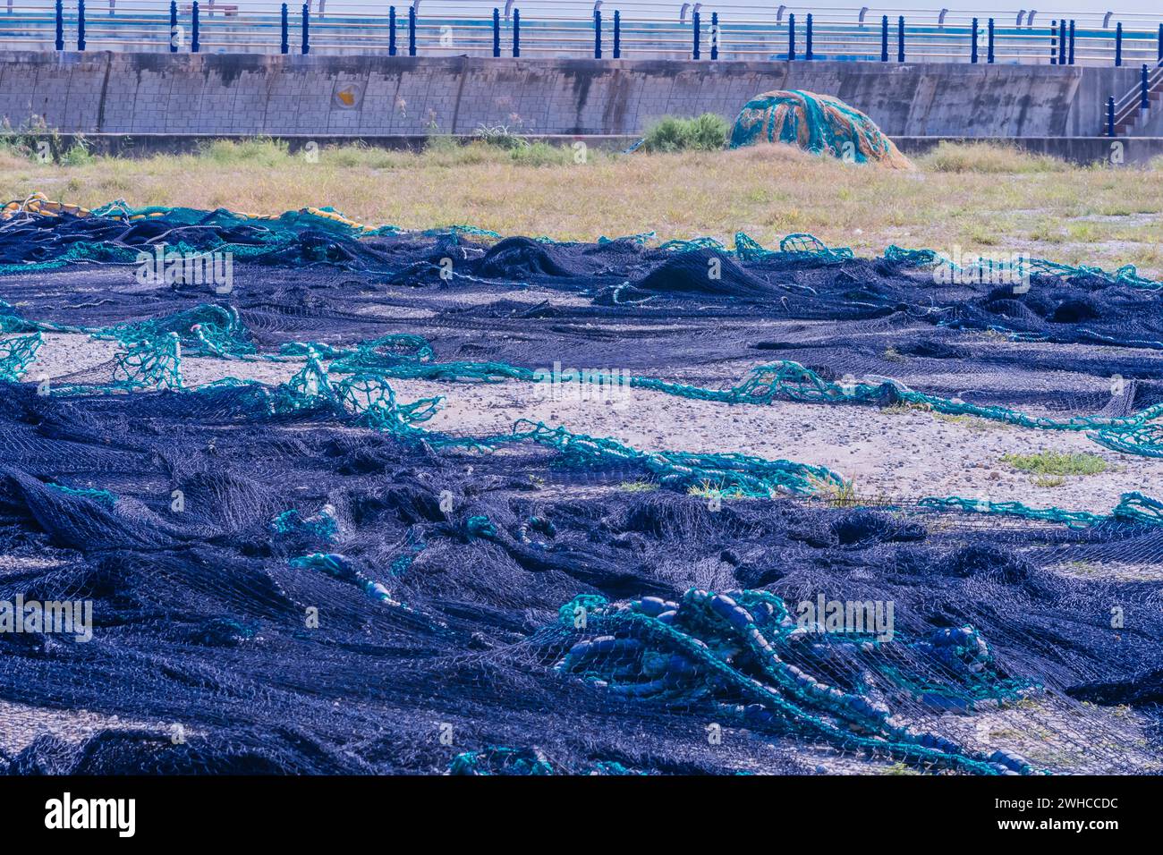 Large black fishing net laid out to dry in gravel lot in front of sea ...