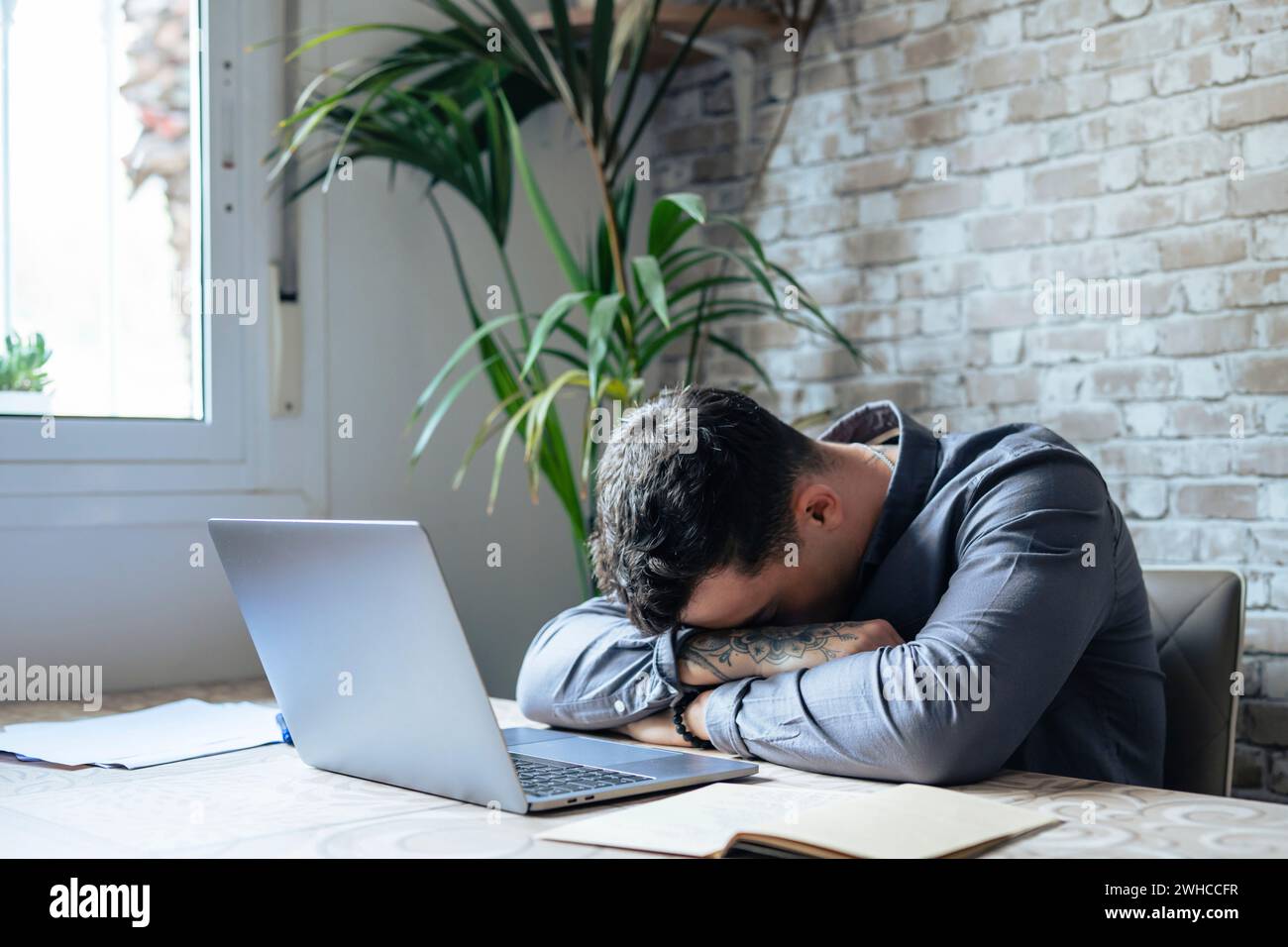 Exhausted young Caucasian male employee sleep desk at office overwork preparing report. Tired ...