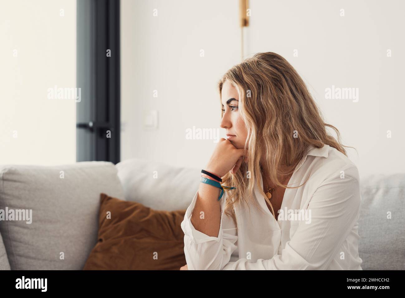 Side view young woman looking away at window sitting on couch at home ...
