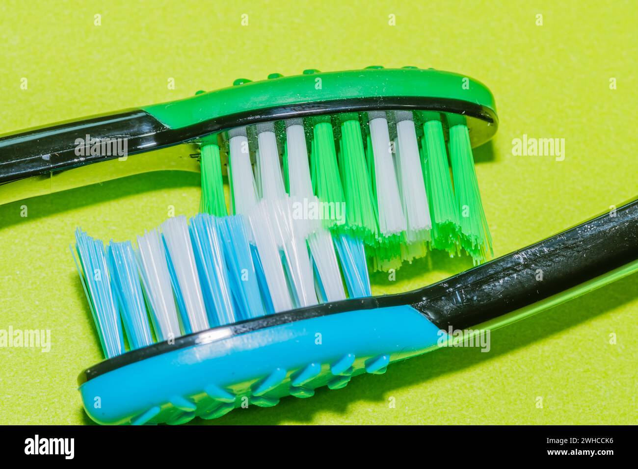 Bristles of one blue and one green toothbrushes interlocked on green ...