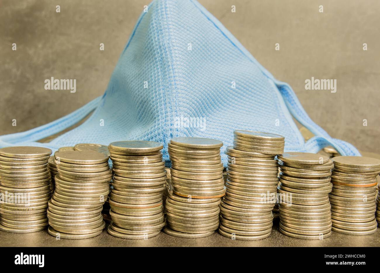 Health face mask laying on top of mound of coins on dark textured ...