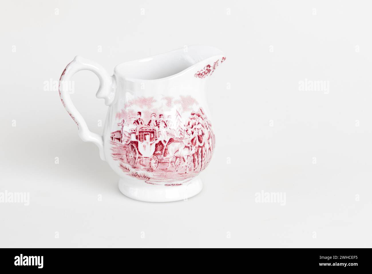 A white ceramic milk jug with a red landscape pattern stands alone ...