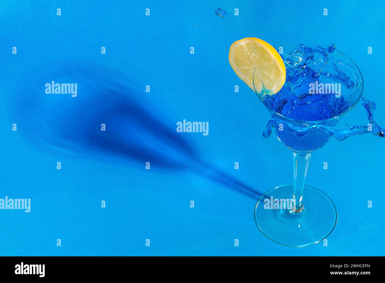 A splashing blue drink with a slice of lemon casts shadows on a blue ...