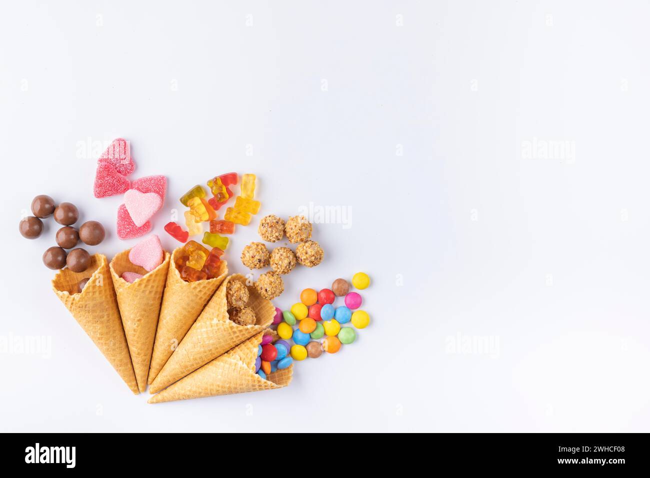 Various sweets in and out of ice-cream cones on a white background ...