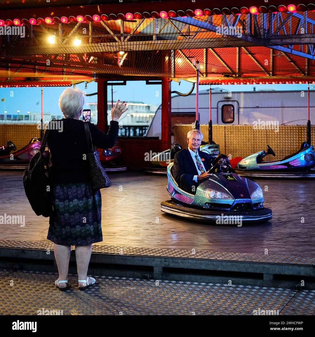 A woman waves to a senior man who is riding the dodgems (bumper cars ...