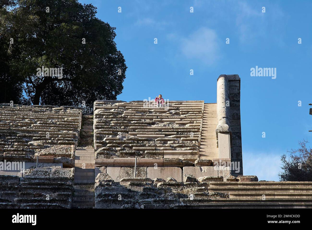 Person sitting alone high up on the stone seats of an ancient theatre ...
