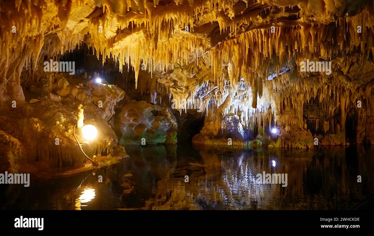 Illuminated cave landscape with water reflection and stalactites from ...