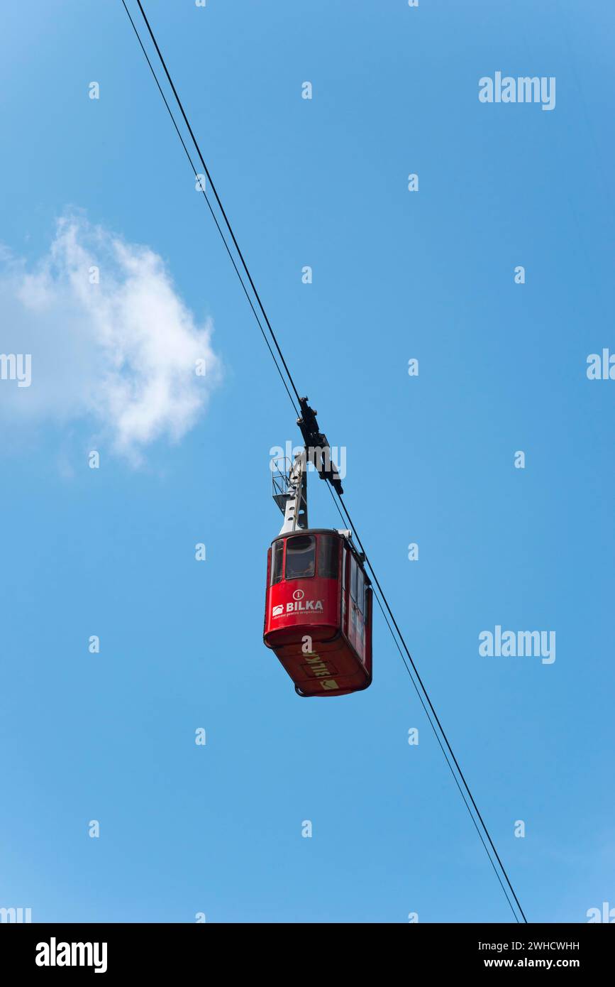 Red cable car gondola hanging on a rope against a clear blue sky with ...