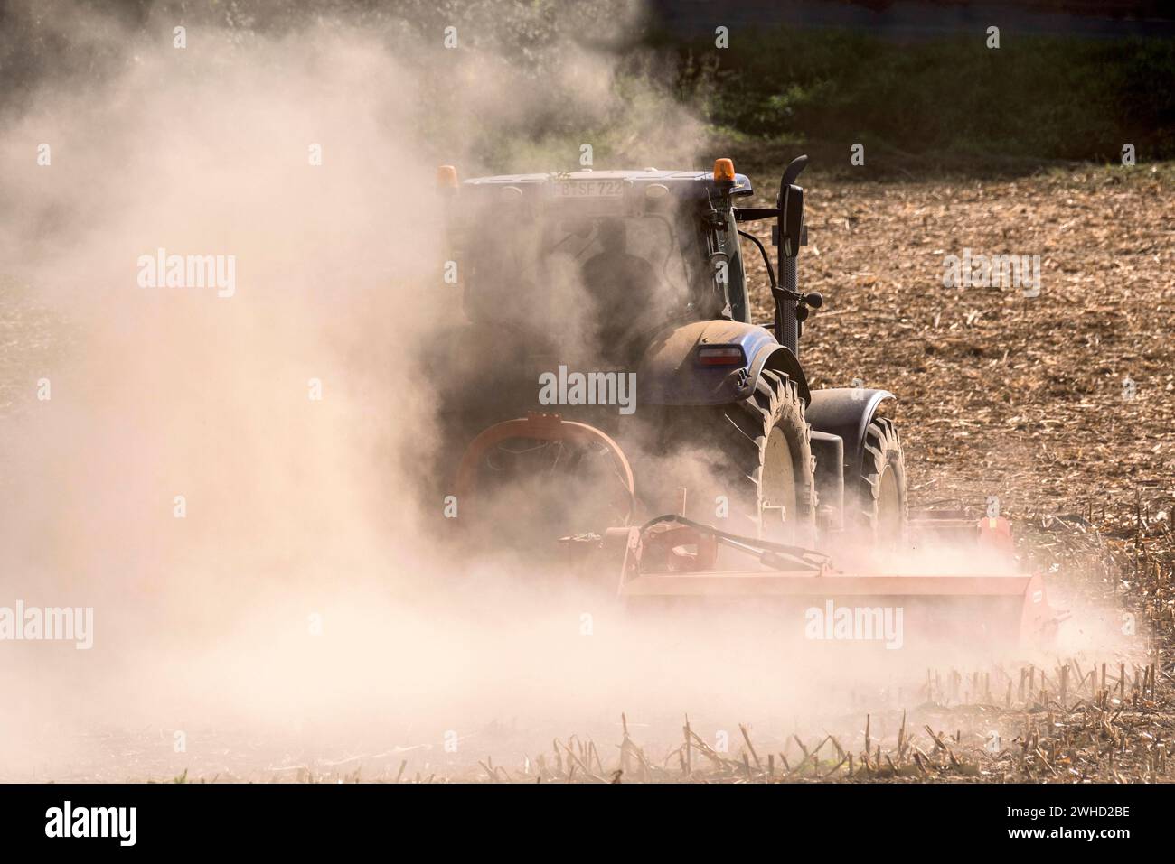 Tractor with plough digging up dried-out soil, large cloud of dust ...