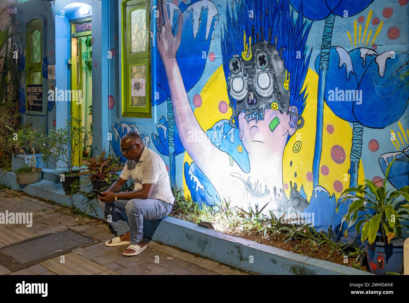 Man sits on a curb in front of illuminated street art in the streets of ...