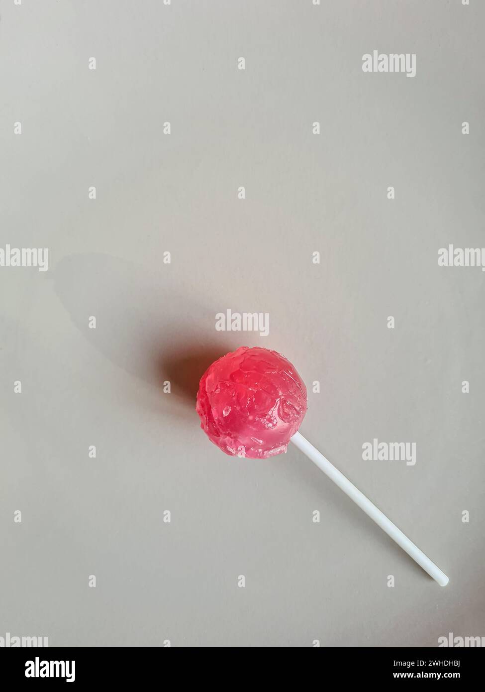 A red lollipop with a stick lies on a plate against a light gray ...