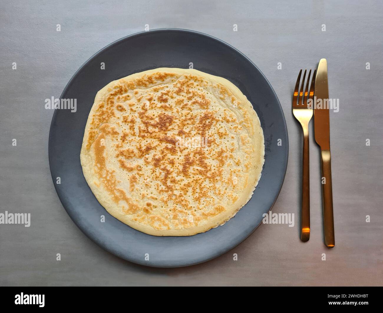 Pancakes on a gray plate with golden cutlery, egg dish with knife and ...
