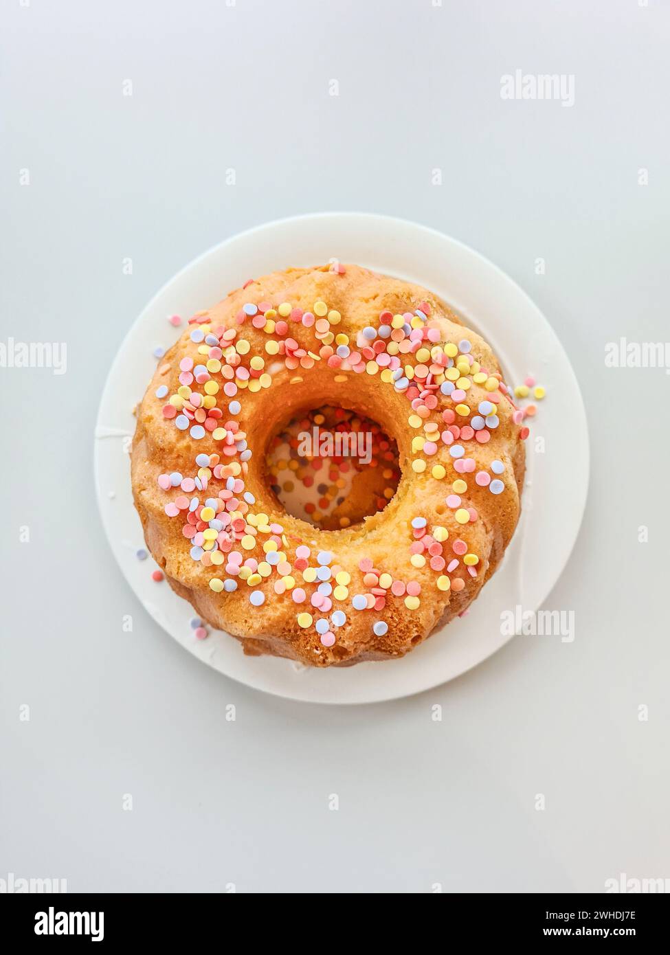 Round sponge cake with colorful sprinkles and topping stands on a white ...