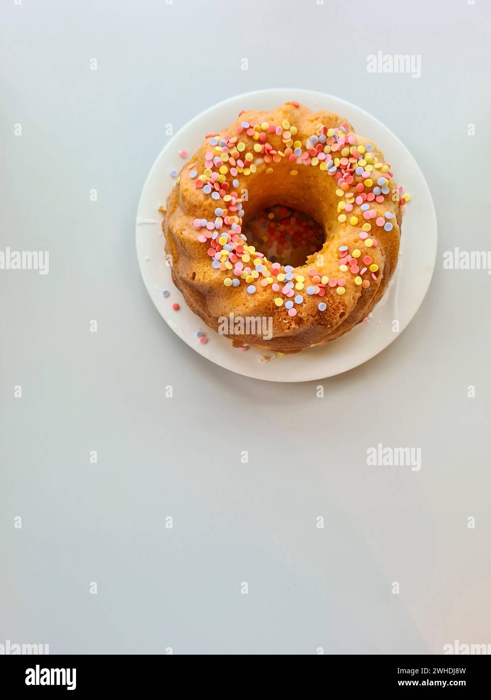 Round sponge cake with colorful sprinkles and topping stands on a white ...