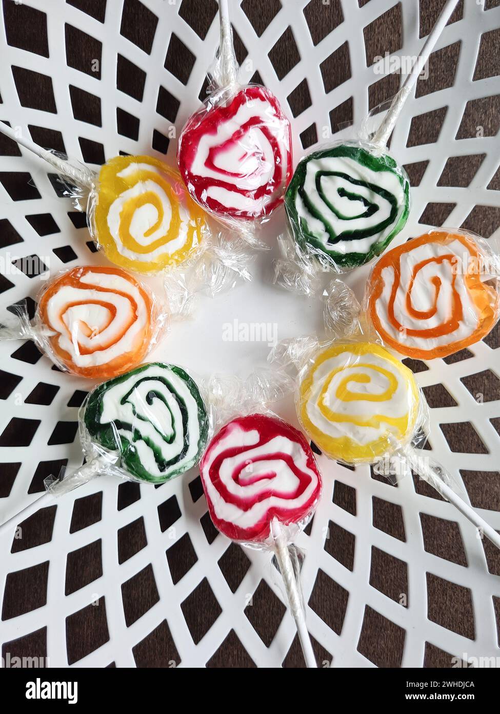 Eight lollies are still wrapped in plastic foil in a circle on a white ...