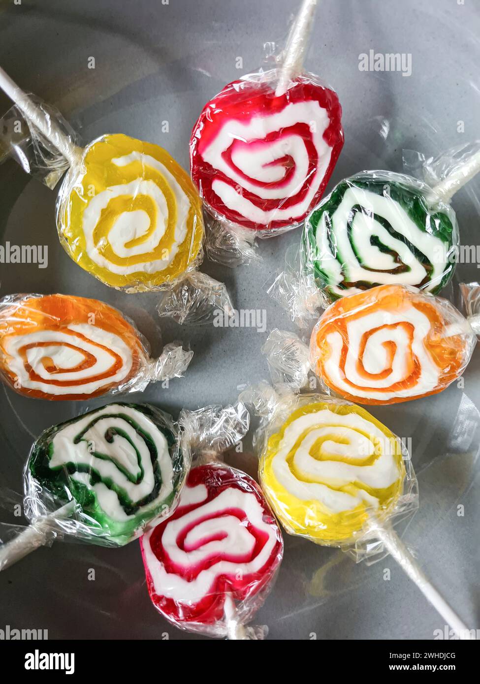 Eight colorful lollipops are still wrapped in plastic foil in a circle ...