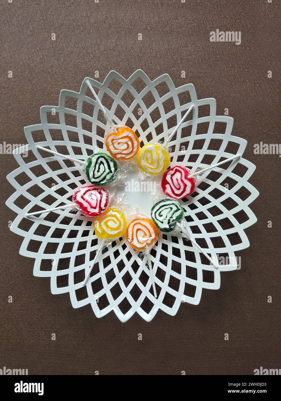 Eight lollies are still wrapped in plastic foil in a circle on a white ...