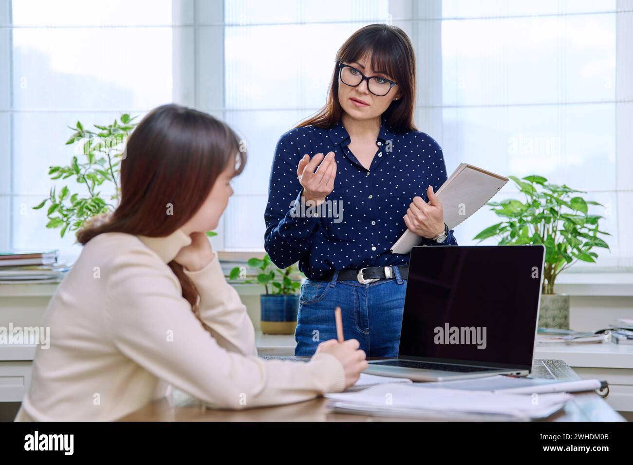 Teenage student studying at desk with computer, trainer mentor helping ...