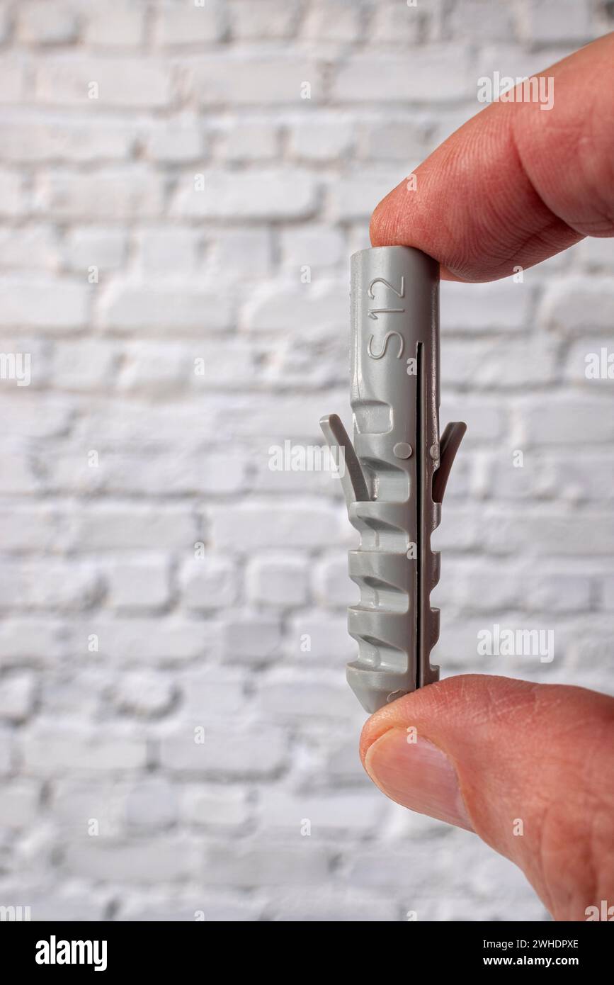 Man's hand holding a fischer expansion plug, detail, background white ...