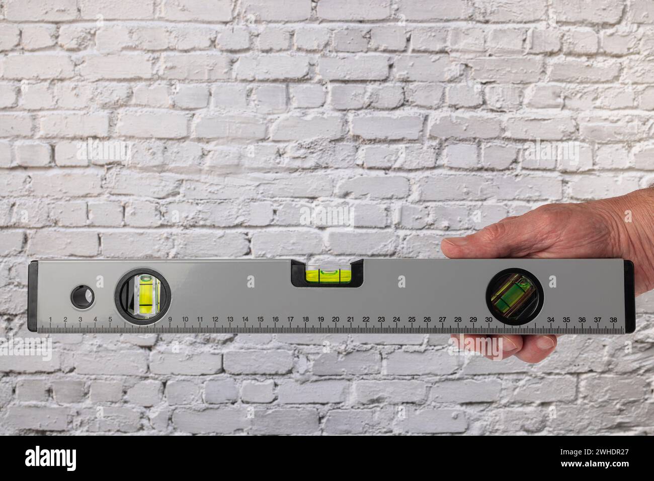 Man's hand holding a spirit level, gray, background white brick wall ...