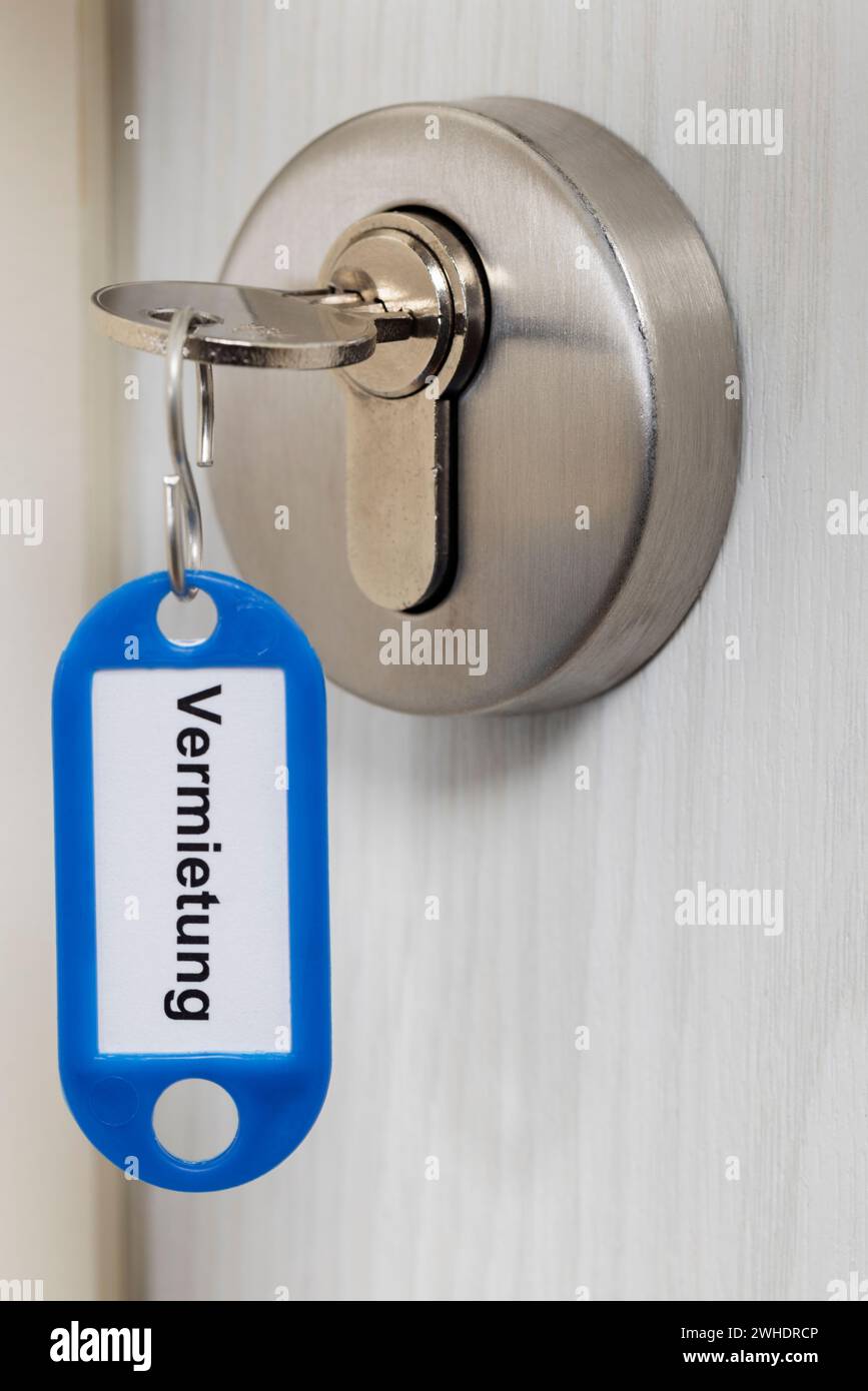Apartment key with blue key ring inserted in door lock, labeled ...