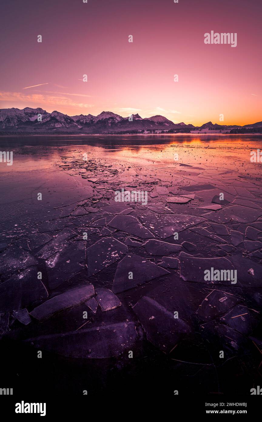 Sunset over the frozen Hopfensee with ice sheets in the foreground and ...