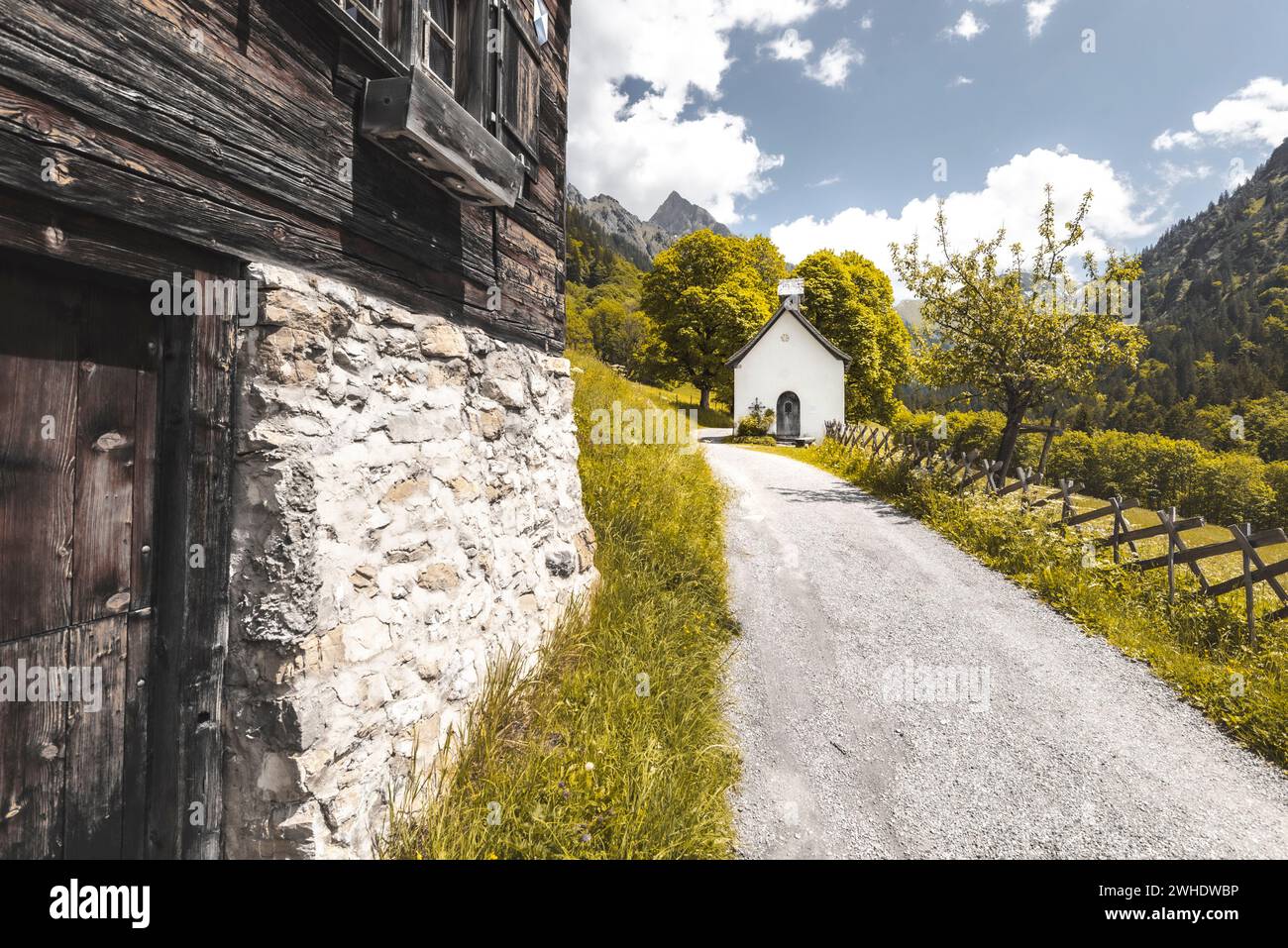 Allgäu mountain farming village in spring. Old mountain hut with small chapel in the background ...