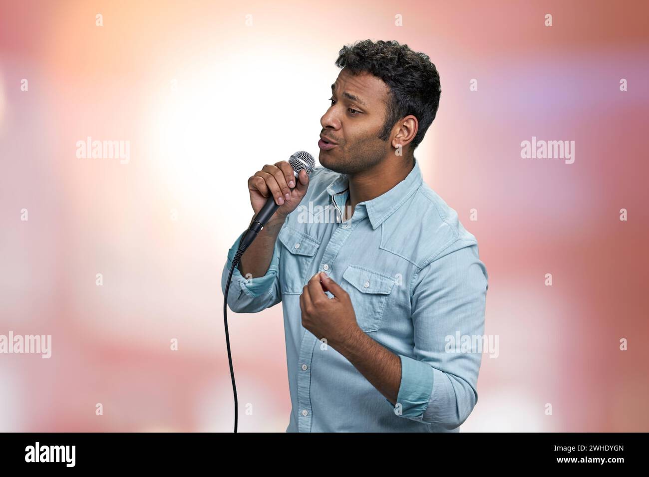 Young indian man performing lyric song on abstract pink bokeh ...