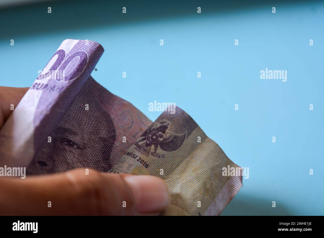 Hand putting Indonesian rupiah money into traditional Indonesian white ...