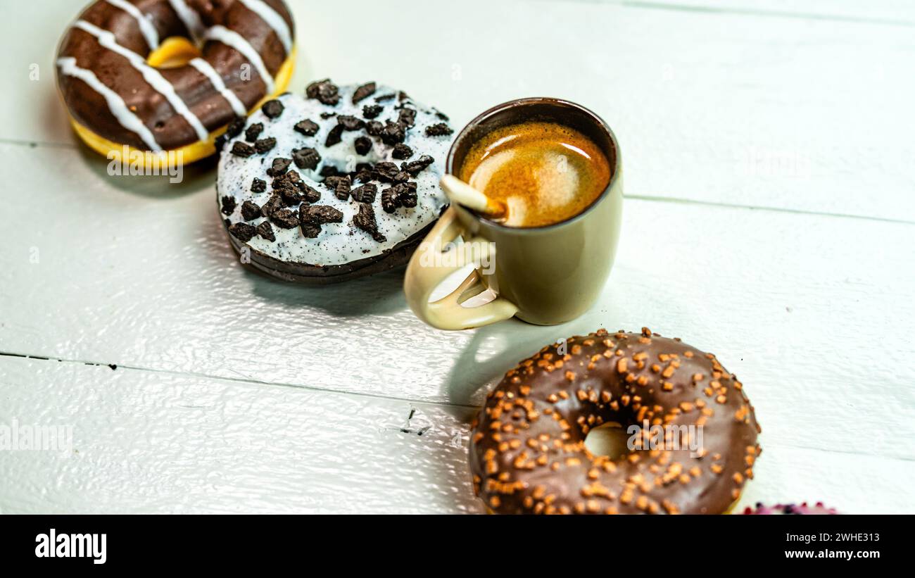 Colorful donuts and coffee cup on white wooden table. Sweet bakery with ...