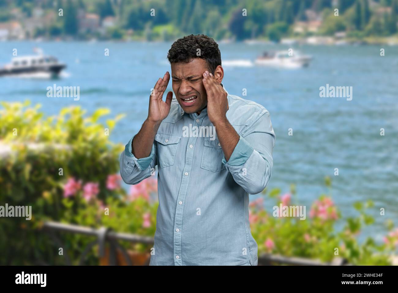 Stressed young man suffering from terrible headache standing outdoors ...