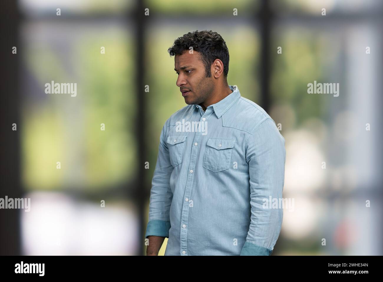 Side view of young sad pensive man on interior blur background. People ...