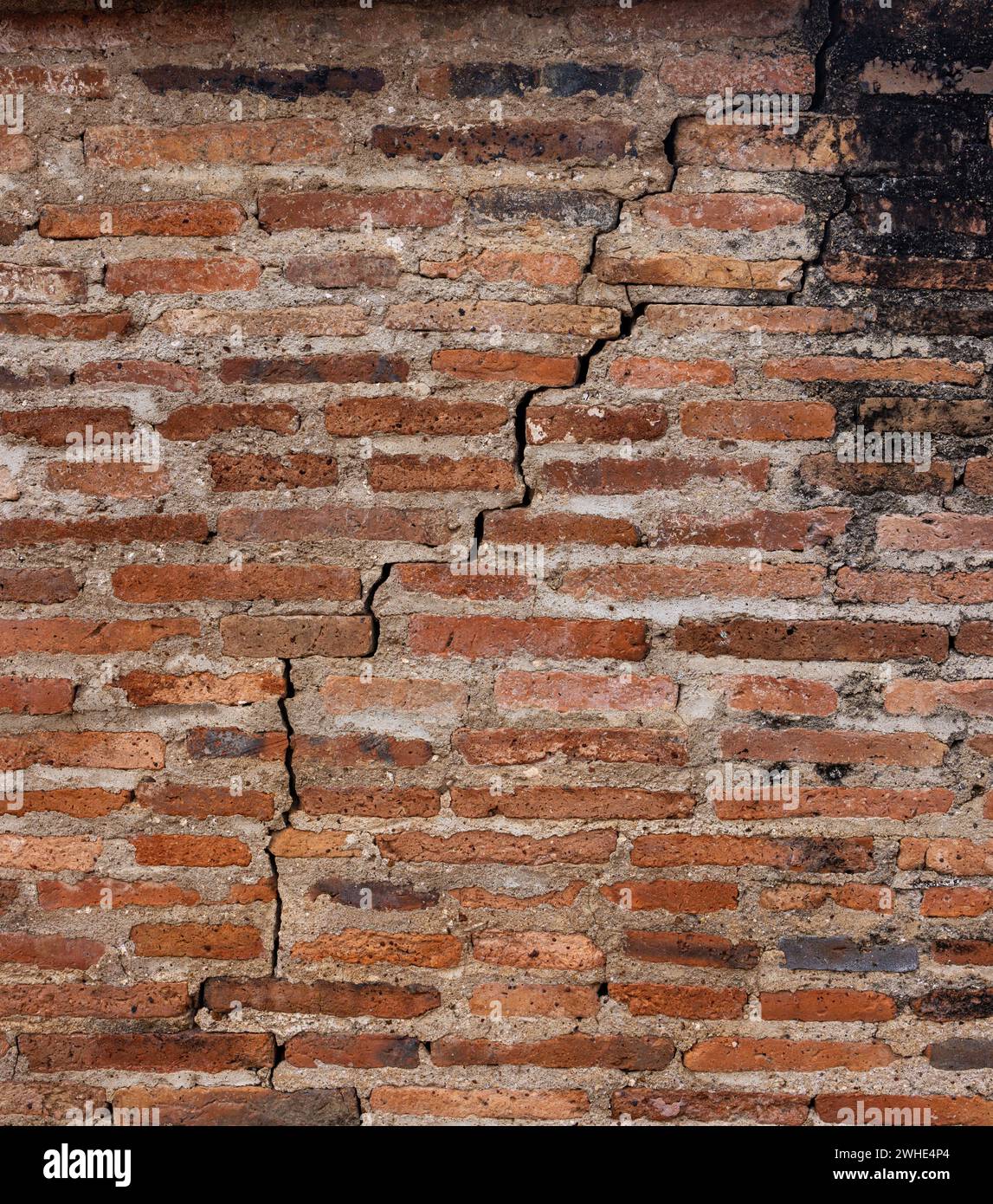 An old red brick wall exhibits a prominent crack running from top to ...