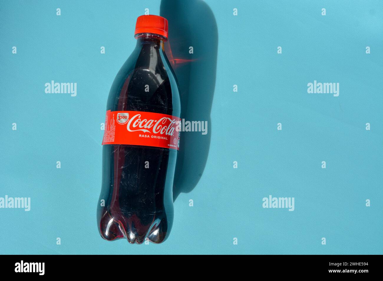 Close up view of a hand holding a Coca Cola product. Against a blue ...