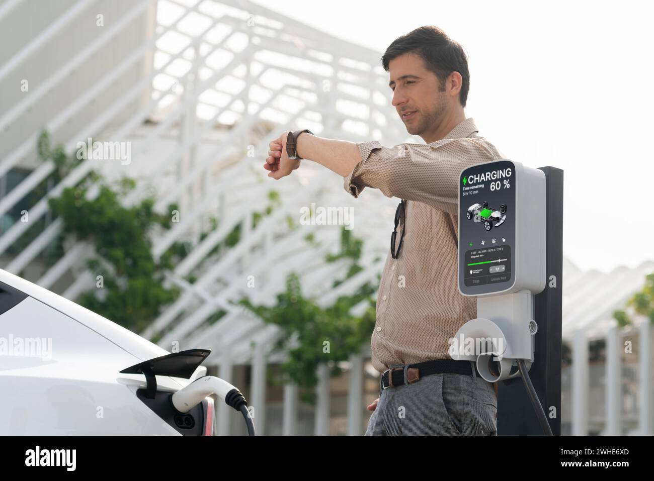 Young man checking time on smartwatch while EV charger to recharging ...