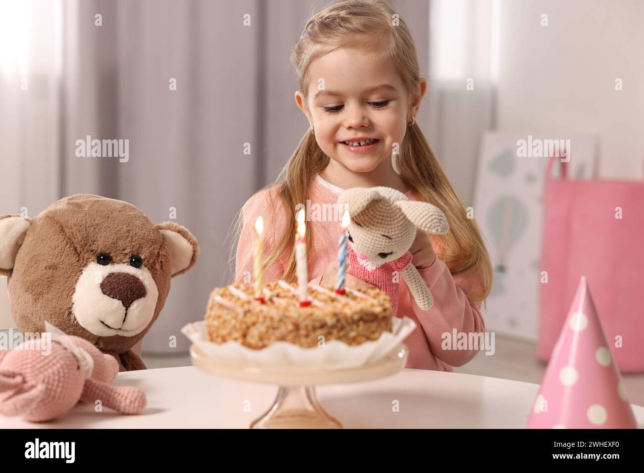 Cute girl with birthday cake and toys at table indoors Stock Photo - Alamy