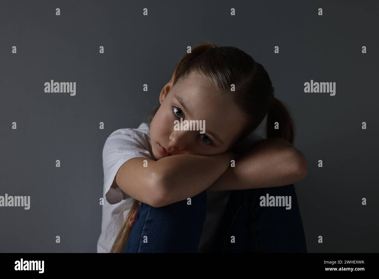 Sad girl sitting near dark grey background Stock Photo - Alamy