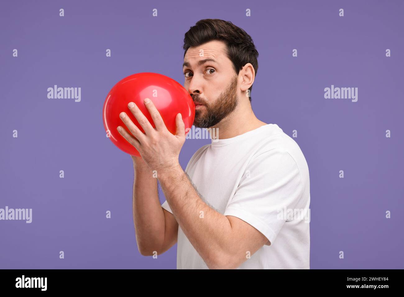 Man inflating red balloon on purple background Stock Photo - Alamy