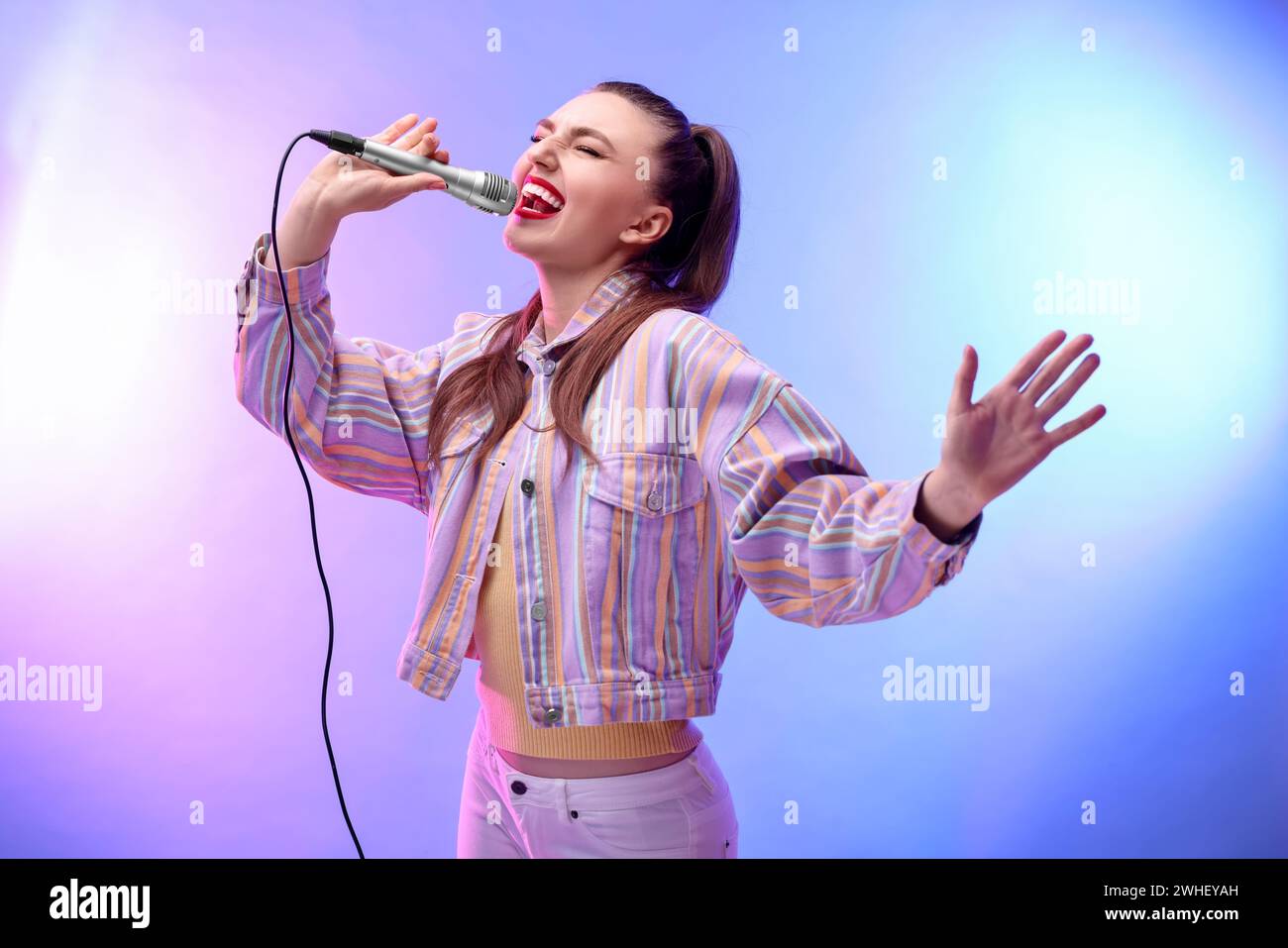 Emotional woman with microphone singing in color lights Stock Photo - Alamy