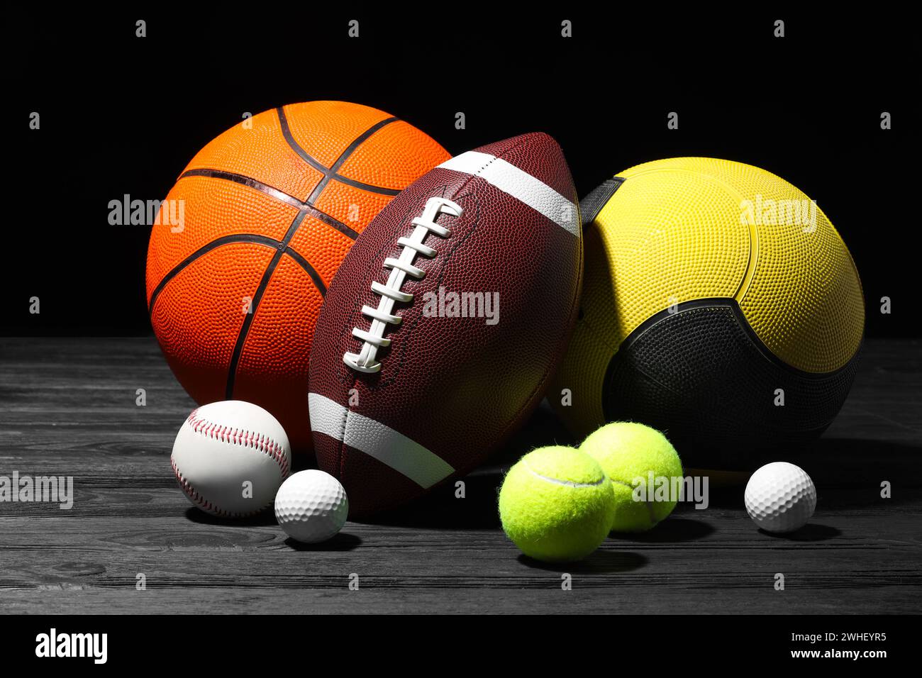 Many different sport balls on dark wooden table against black ...