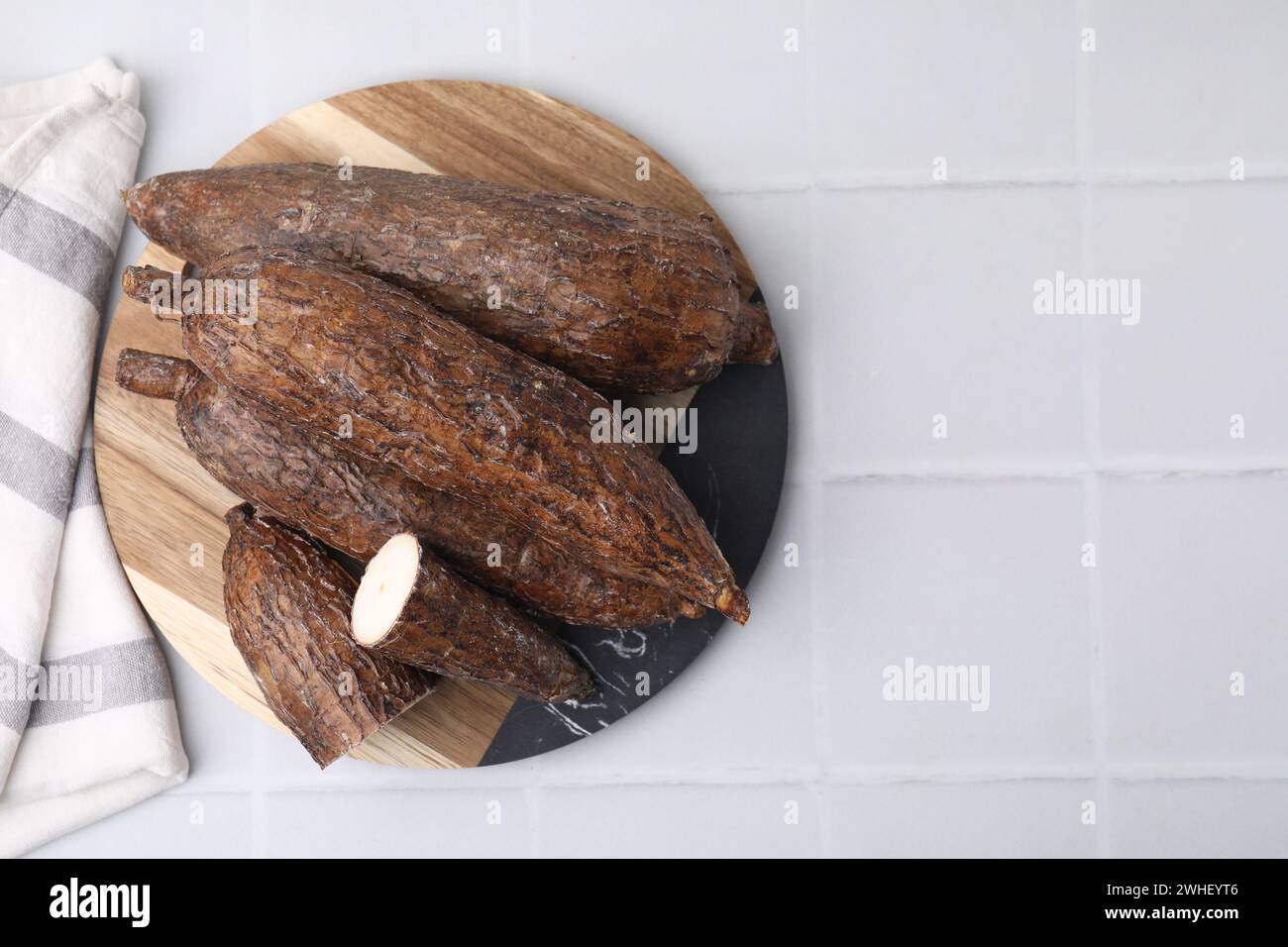 Whole and cut cassava roots on white tiled table, top view. Space for ...