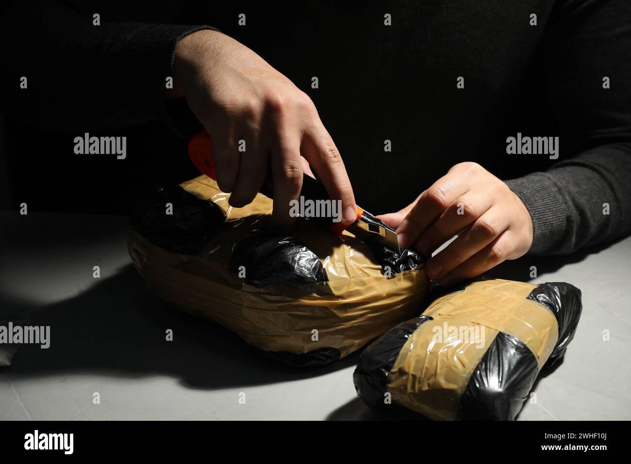 Smuggling and drug trafficking. Man opening package of narcotics with ...