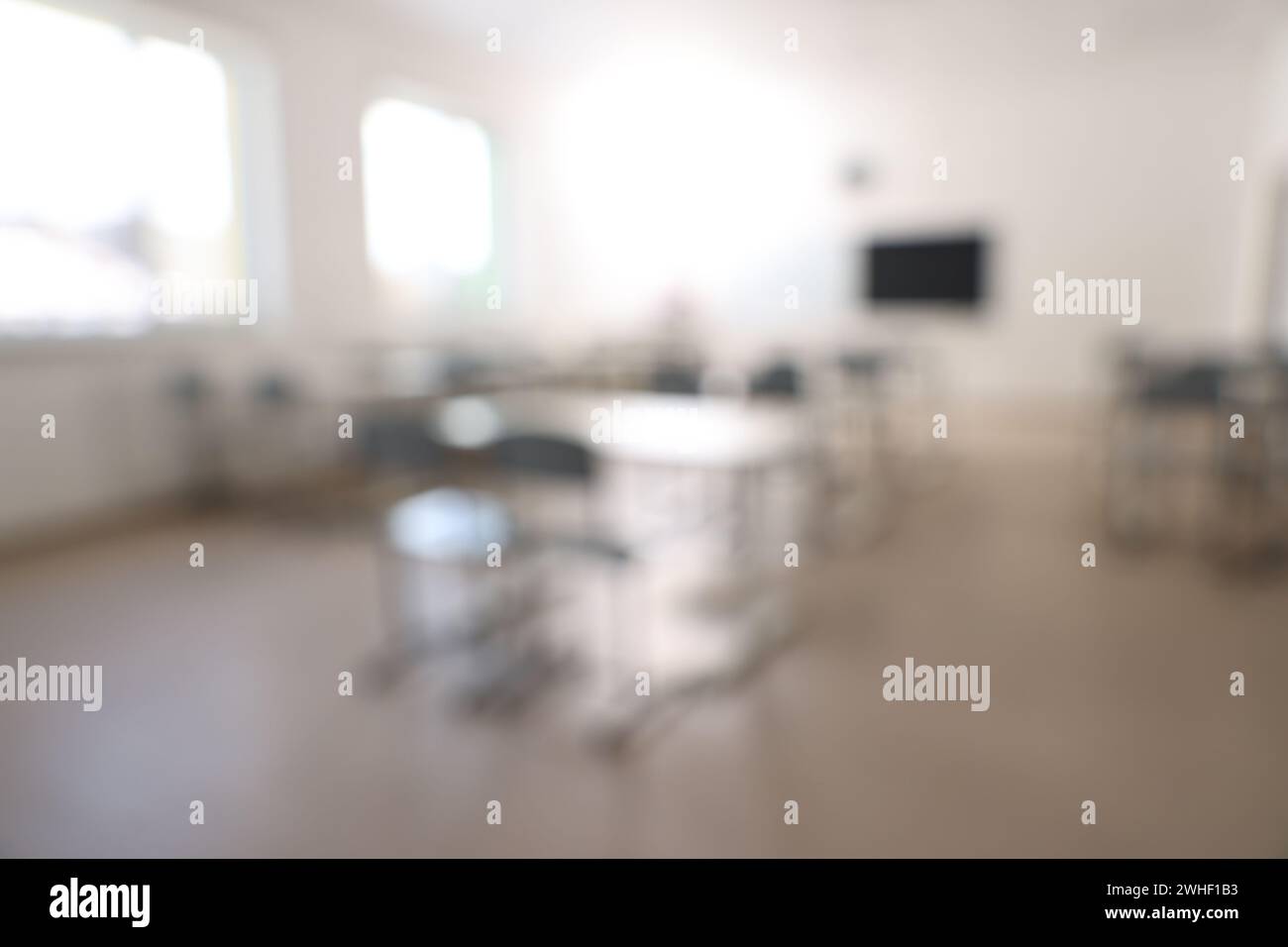 Blurred view of empty school classroom with desks, windows and chairs ...