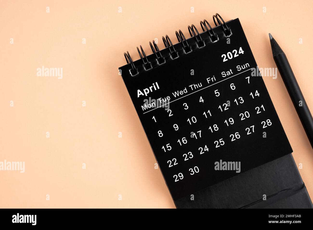 April 2024 Black spiral desktop calendar and wooden pencil on yellow ...