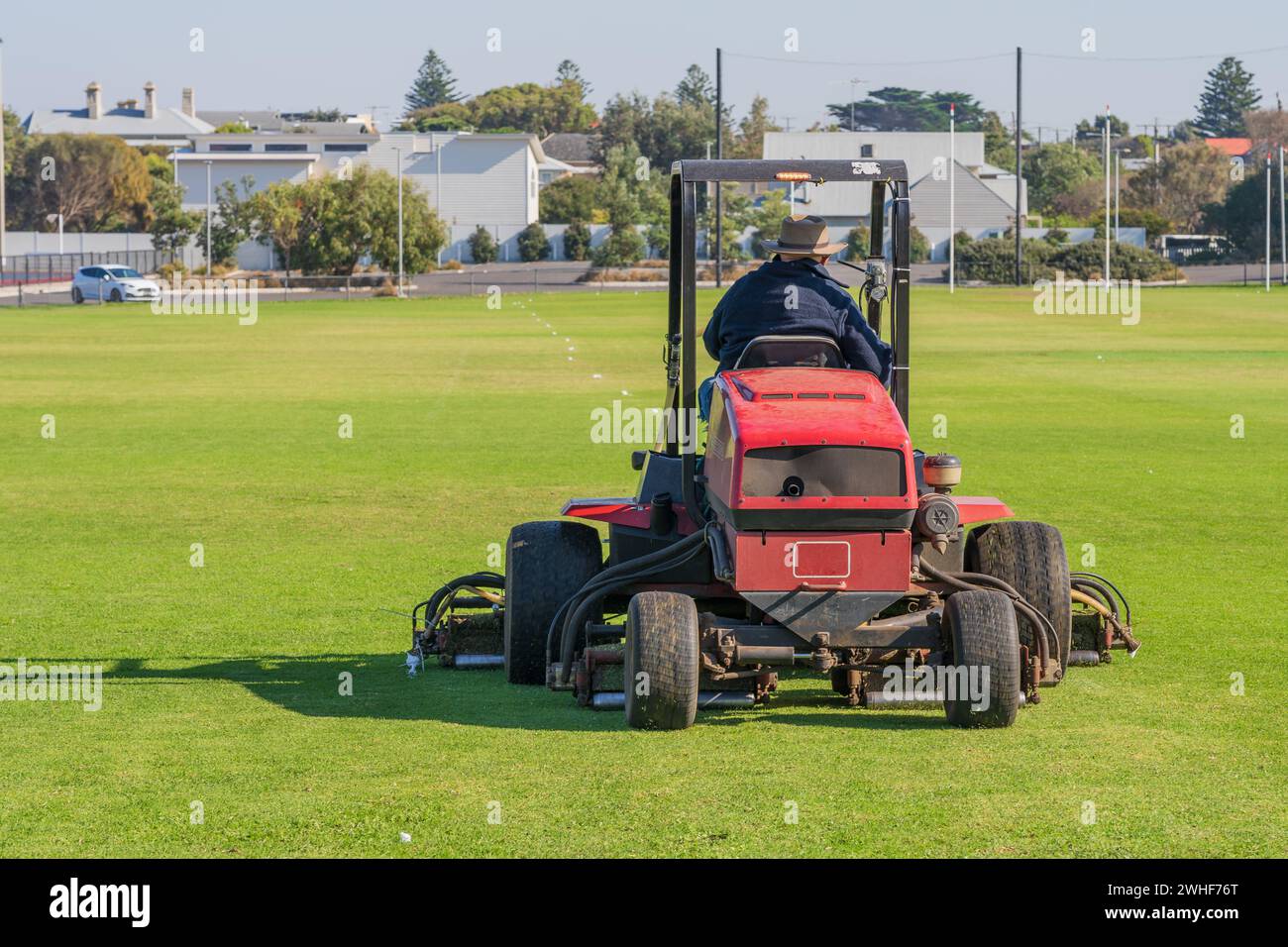 Rear view of a greenskeeper on a large rider mower mowing a green ...